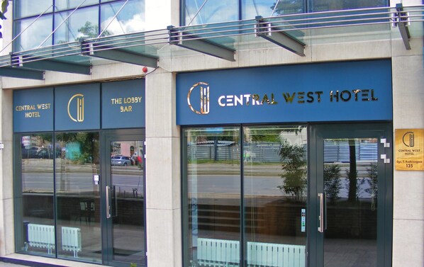 Exterior do Hotel Central West, com entrada visível, portas de vidro e placa indicando The Lobby Bar.