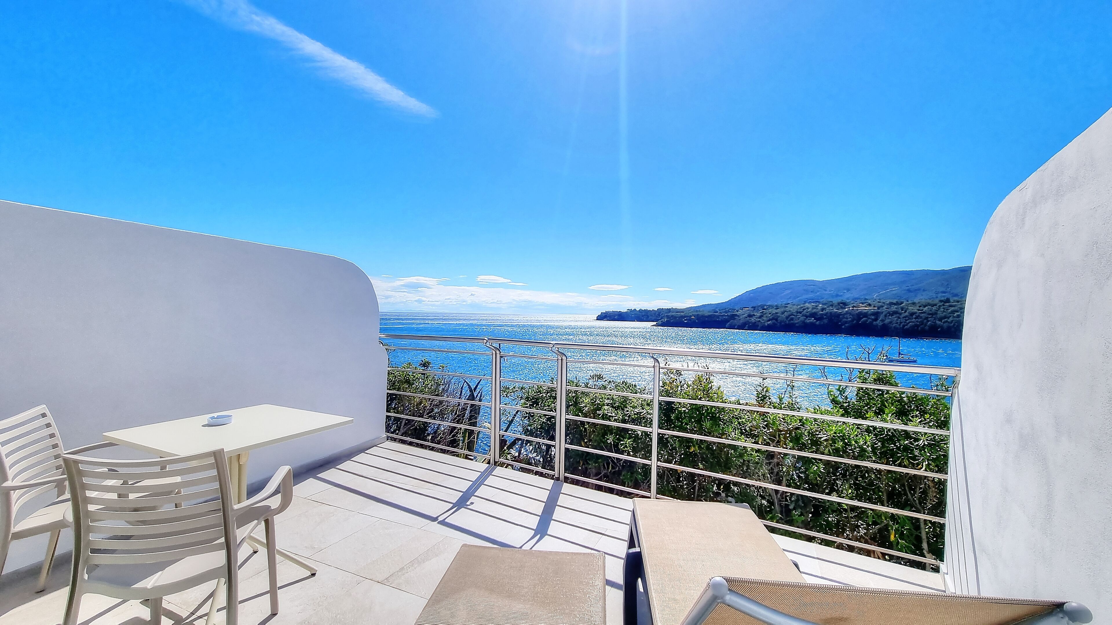 Varanda com mesa e cadeiras, com vista para a costa e céu claro.