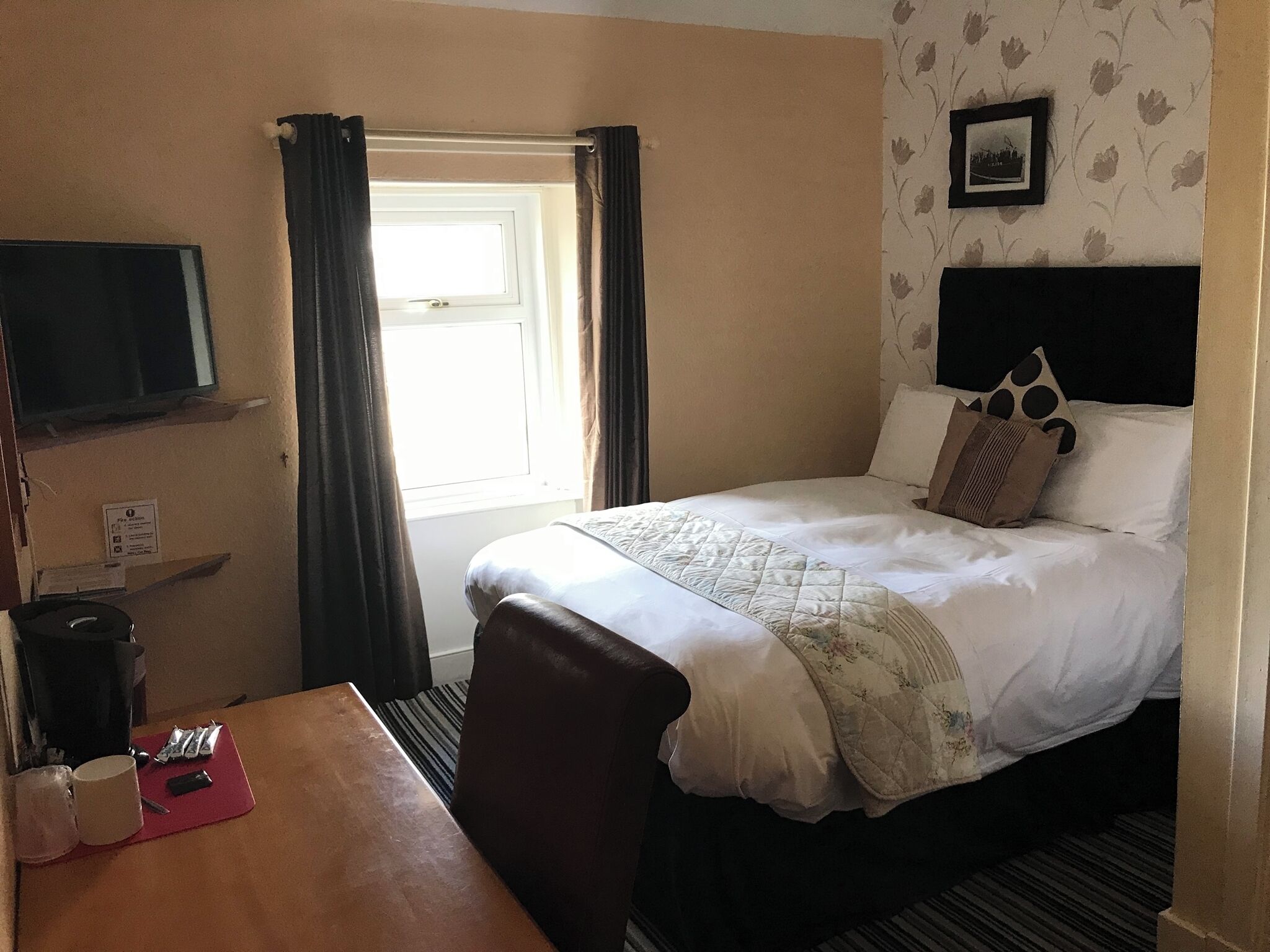 Quarto de hotel com cama, televisão, mesa com caneca e telefone, e janela com cortinas.