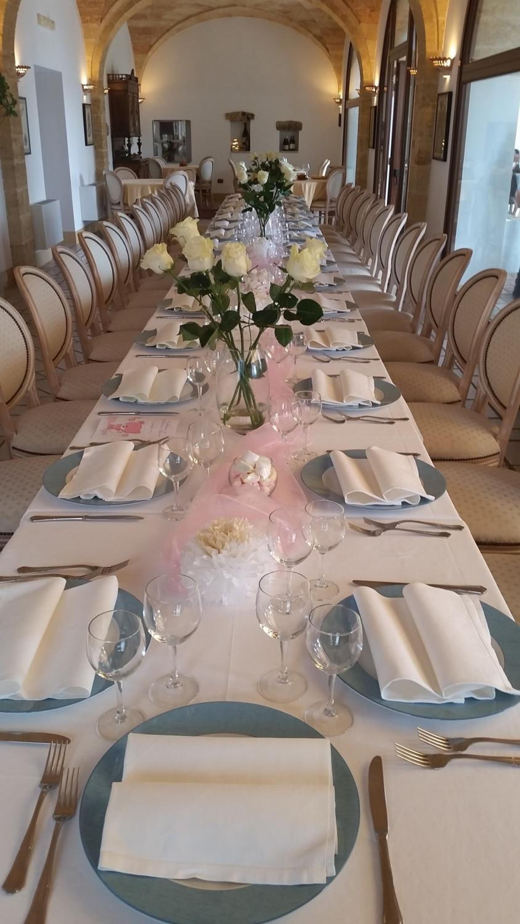 Uma longa mesa de jantar montada para um evento formal, com cadeiras em ambos os lados e um arranjo floral no centro.