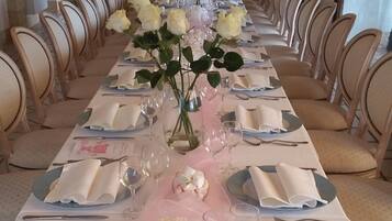 Uma longa mesa de jantar montada para um evento formal, com cadeiras em ambos os lados e um arranjo floral no centro.