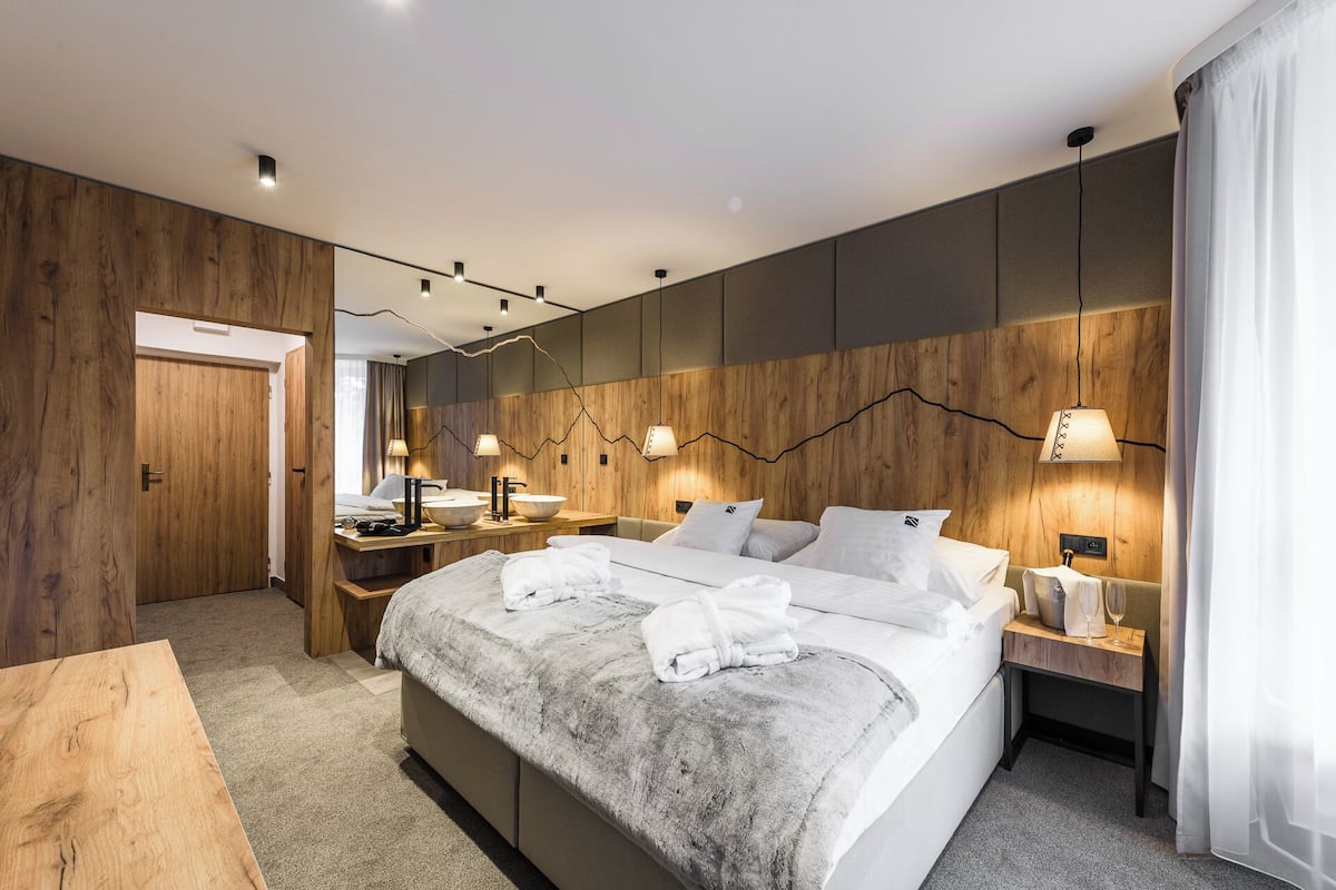 Quarto de hotel moderno com uma cama grande, paredes de painel de madeira e um espelho.