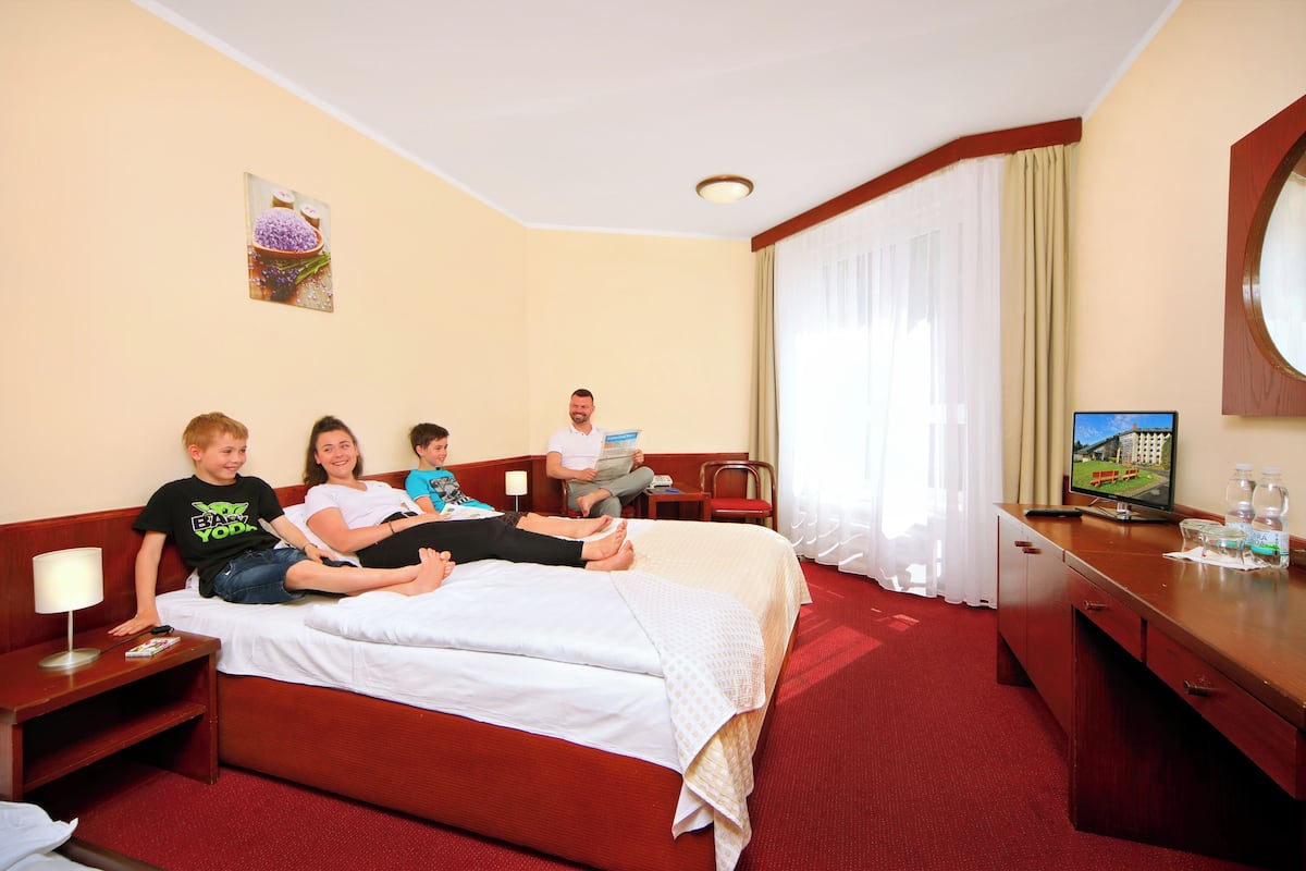Quarto de hotel com cama, escrivaninha, computador, televisão e janela com cortinas.