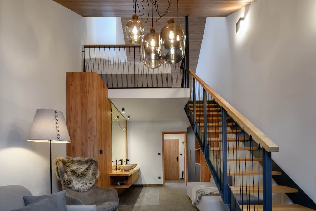 Uma sala de estar moderna com um sofá, um abajur, um cobertor de pele e uma escada com corrimão de madeira.