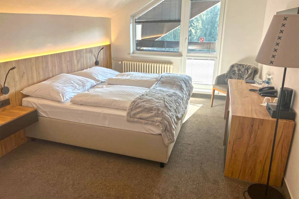 Quarto com cama, mesas de cabeceira, escrivaninha e uma cadeira.