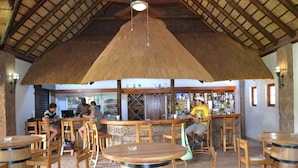 Um espaço de bar rústico com móveis de madeira, telhado de palha e adega.