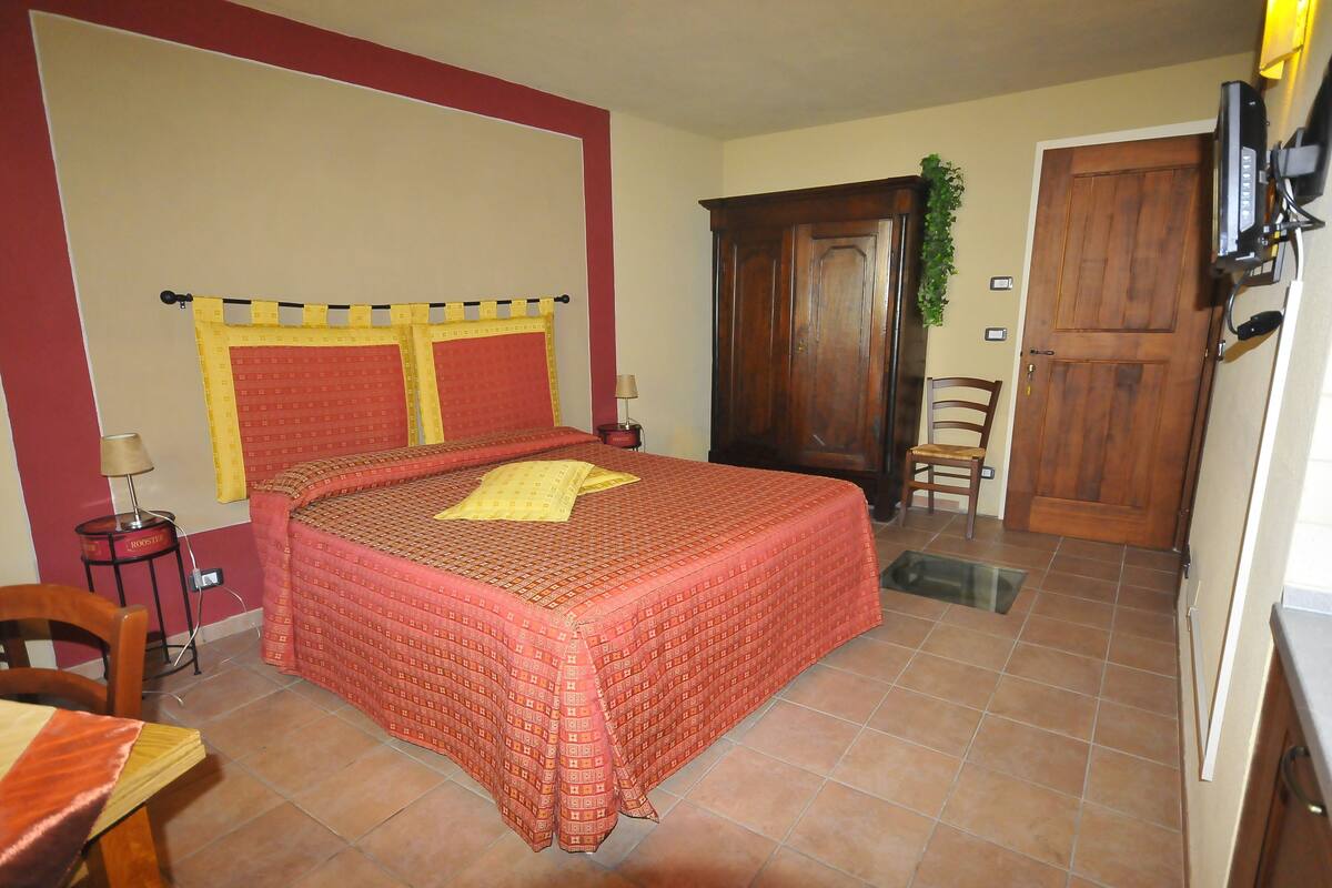Quarto com uma cama, guarda-roupa de madeira, uma cadeira, uma mesa e uma porta.