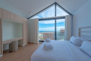 Quarto de hotel moderno com uma janela ampla, cama bem arrumada, guarda-roupa de madeira e uma pequena lixeira.