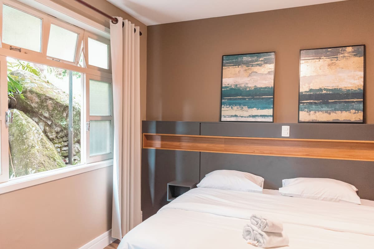 Quarto de hotel com cama, janela com cortinas e duas pinturas penduradas na parede.