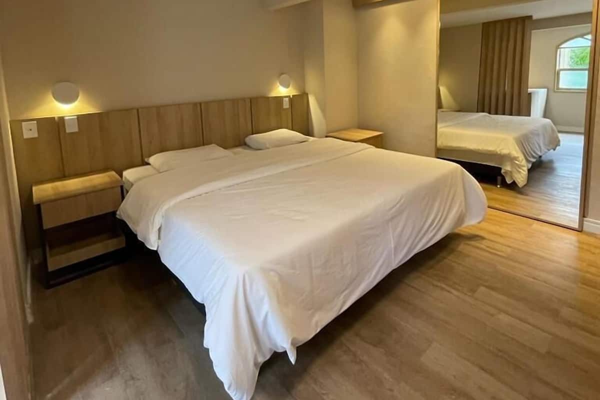Quarto com uma cama grande, mesas de cabeceira, um espelho e piso de madeira.