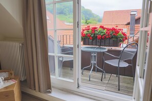 Varanda com mesa e cadeiras, vista de flores vermelhas e um prédio com telhado vermelho.