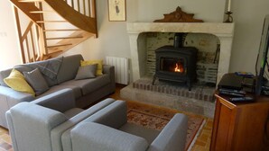 Uma sala de estar com sofá cinzento, lareira, escada de madeira e televisão em um armário de madeira.