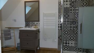 Casa de banho com chuveiro, pia com espelho, porta-toalhas e azulejos estampados.