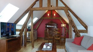 Quarto estilo loft com teto de madeira, televisão, mesa de jantar e sofá.