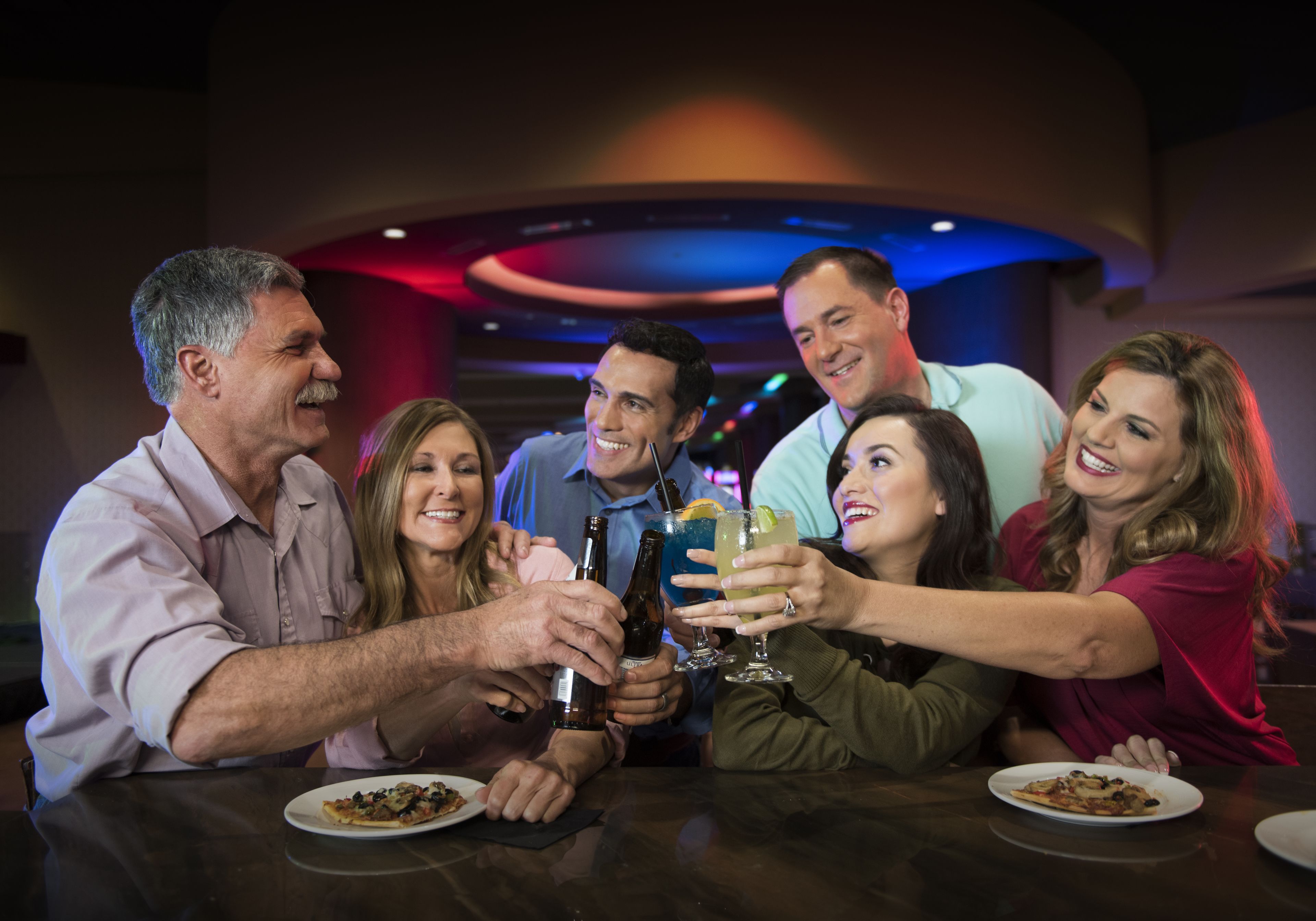 Um grupo de pessoas brindando com bebidas à mesa em ambiente interno com pouca luz.