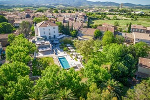Vista aérea de um bairro residencial com uma casa grande e branca, piscina e vegetação ao redor.
