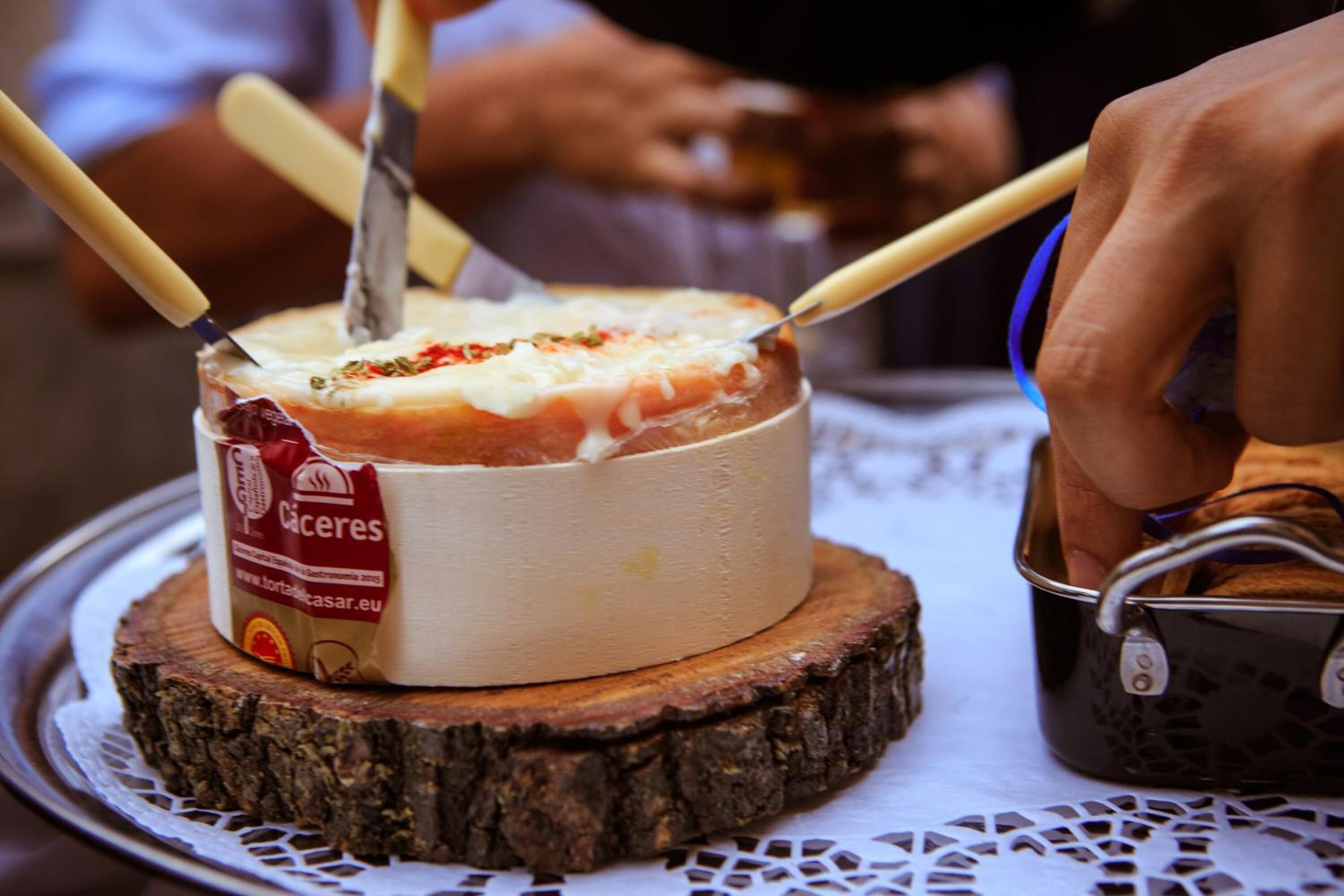 Um queijo redondo sobre uma tábua de madeira com uma faca e um garfo.
