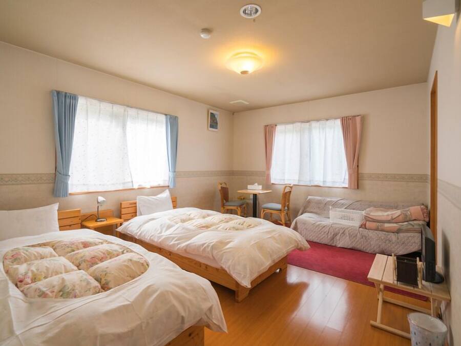 Quarto de hotel com duas camas, uma mesa pequena, uma cadeira e uma escrivaninha com um computador.