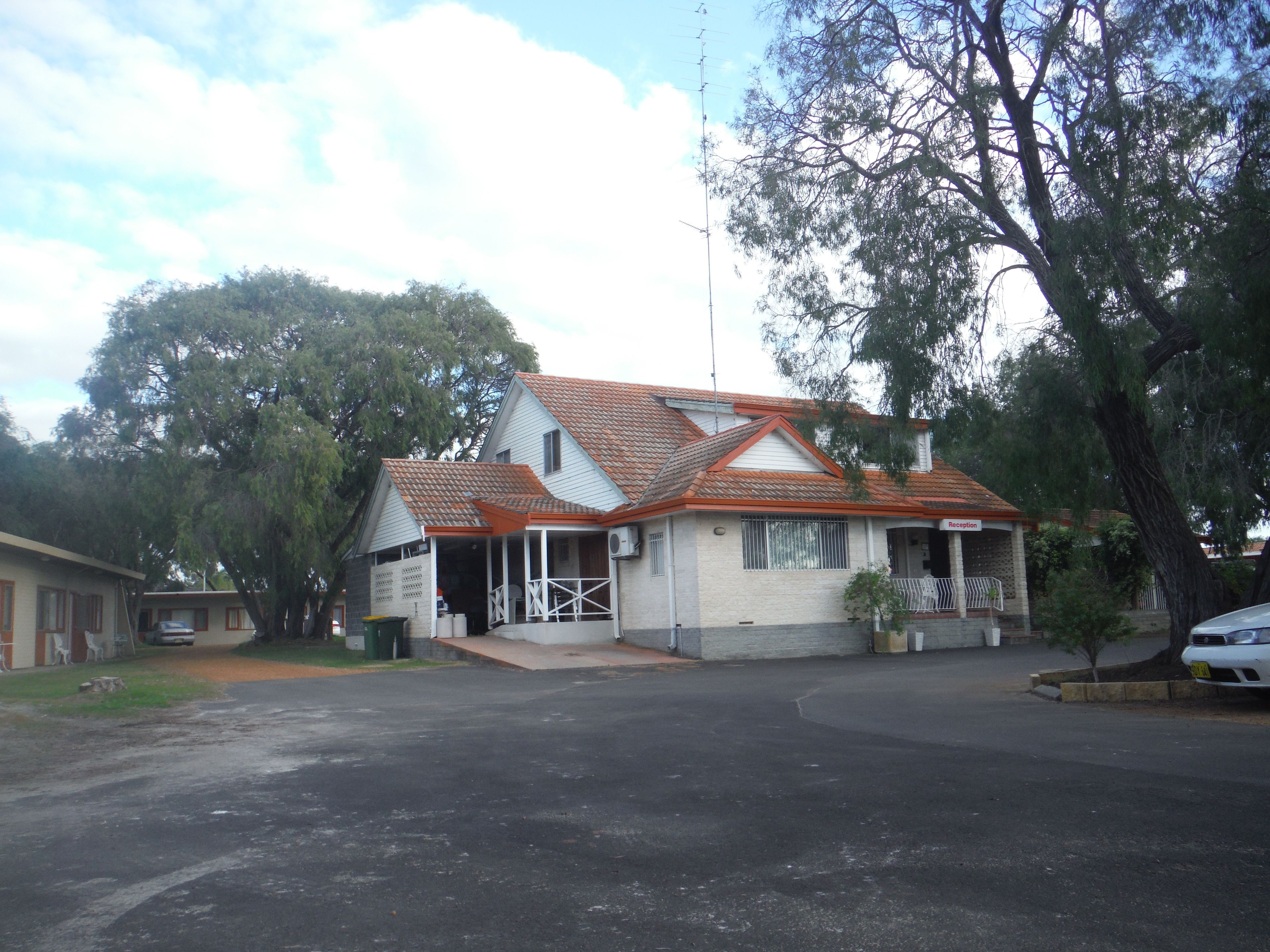 Uma casa de dois andares com telhado de telhas vermelhas, varanda coberta e um pequeno jardim.