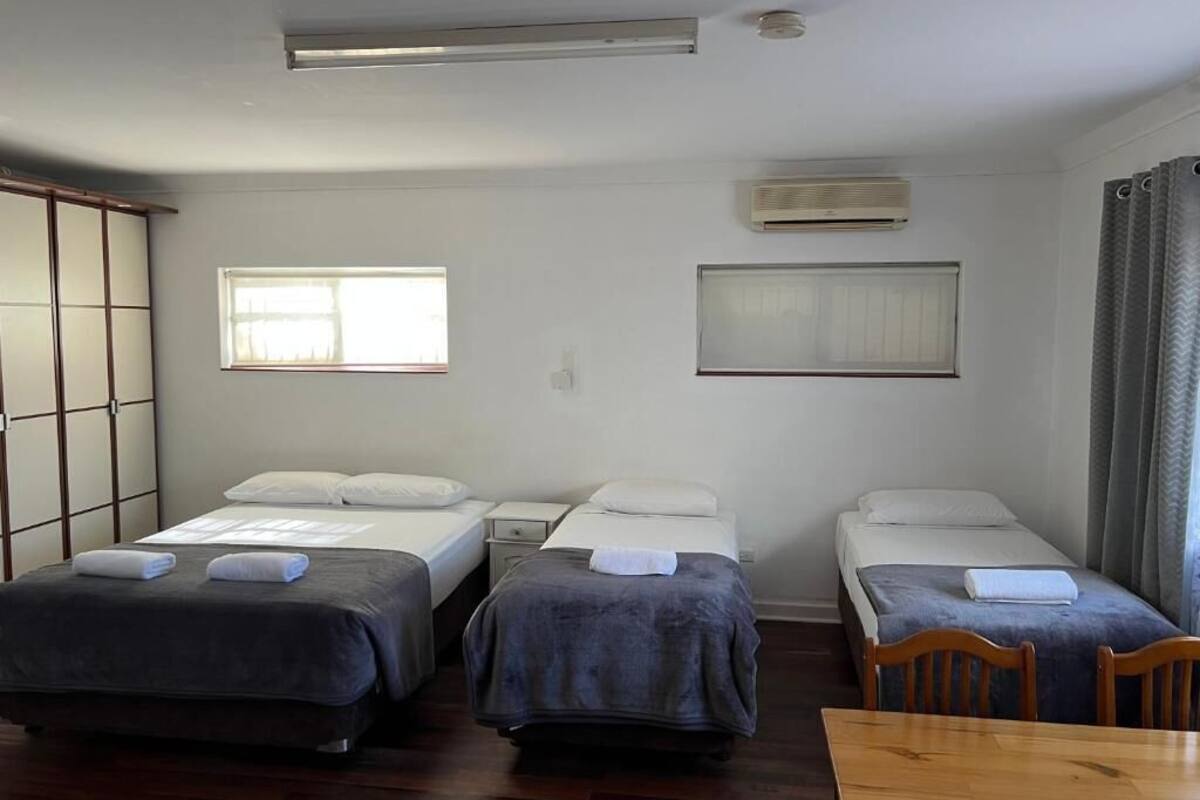 Quarto de hotel com três camas de solteiro, uma mesa de madeira e uma porta de correr.