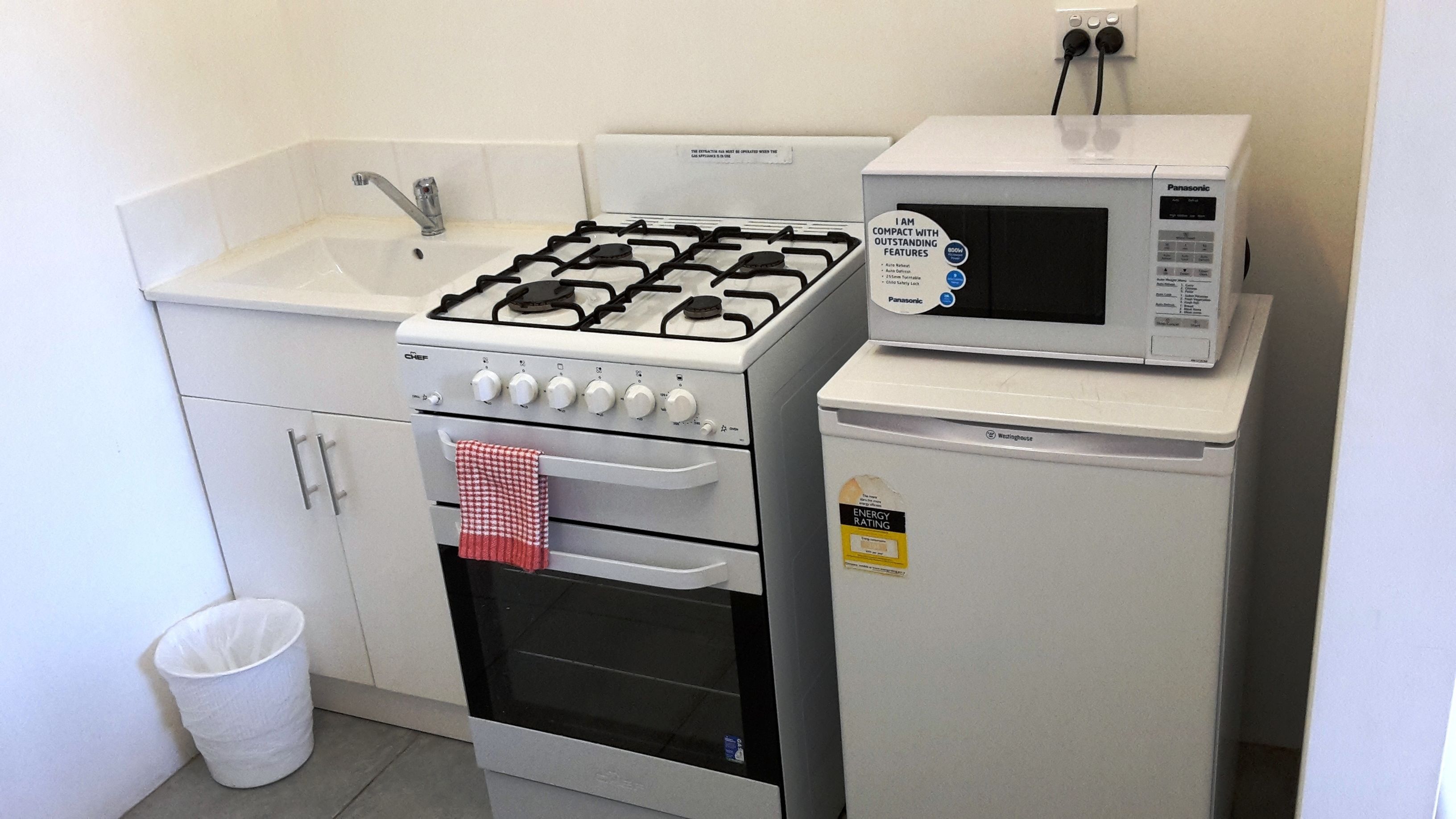Cozinha compacta com fogão a gás, forno, micro-ondas e pia.