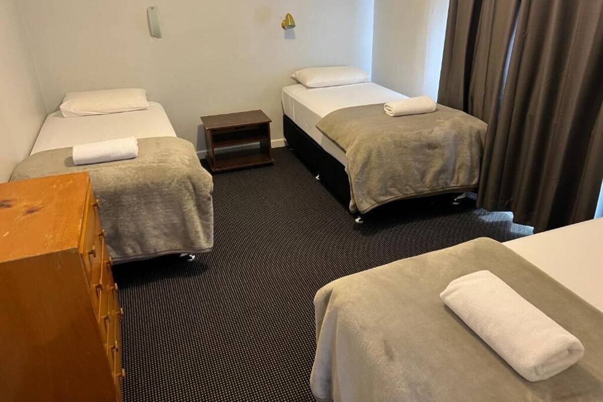 Quarto de hotel com duas camas de solteiro, penteadeira de madeira e uma mesinha.