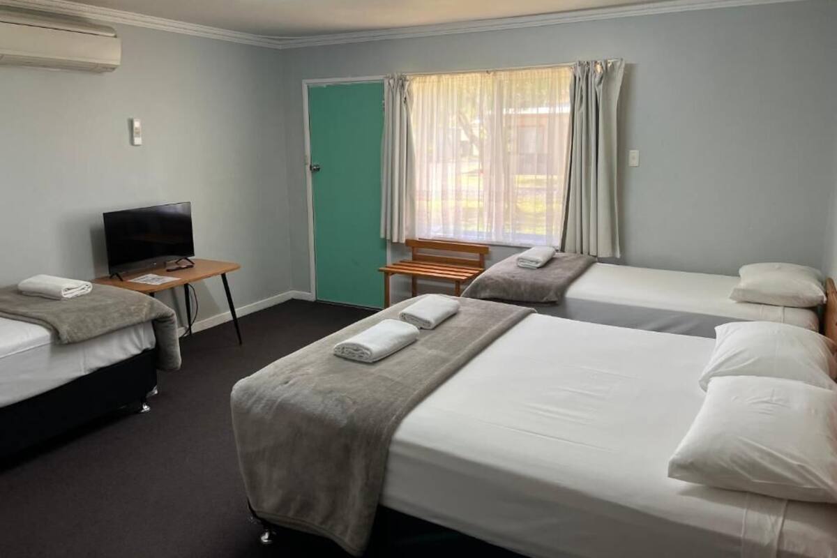 Quarto de hotel com duas camas, televisão, mesa pequena e janela com cortinas.
