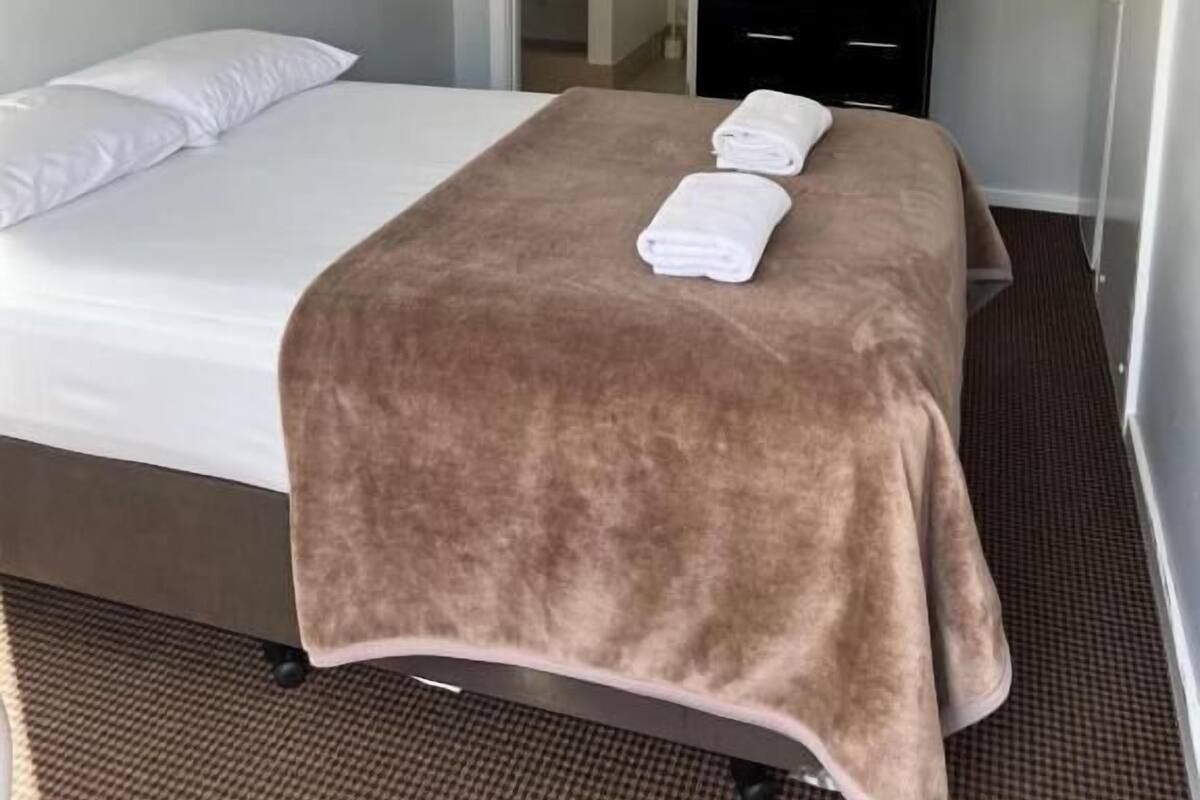 Quarto de hotel com cama, televisão, escrivaninha e chuveiro.