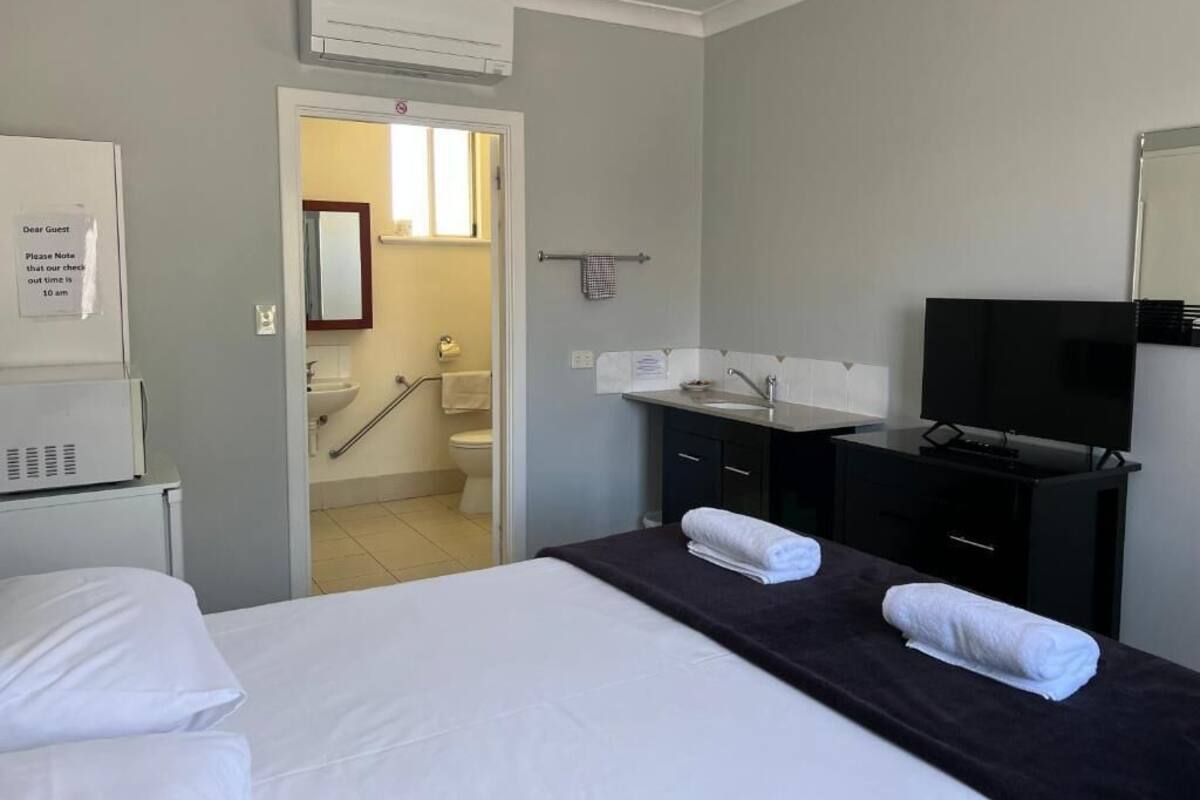 Quarto de hotel com cama, televisão, escrivaninha e banheiro visível por uma porta aberta.
