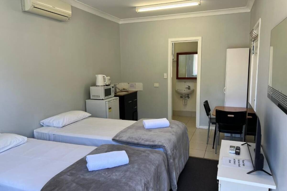 Quarto de hotel com duas camas, uma escrivaninha, uma cadeira, micro-ondas, frigorífico, pia e espelho.