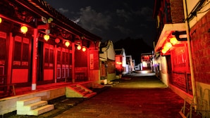 Um beco estreito com arquitetura tradicional, iluminado por luzes vermelhas, que leva a um edifício com entrada visível.