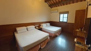 Quarto de hotel com duas camas, piso de madeira, teto de madeira, televisão e janela.