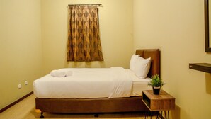 Cama bem arrumada com lençóis brancos, cabeceira marrom e uma pequena planta em vaso sobre uma mesinha de cabeceira de madeira.