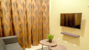 Uma sala de estar com sofá, duas mesas redondas, TV de tela plana na parede e cortina estampada com flores.