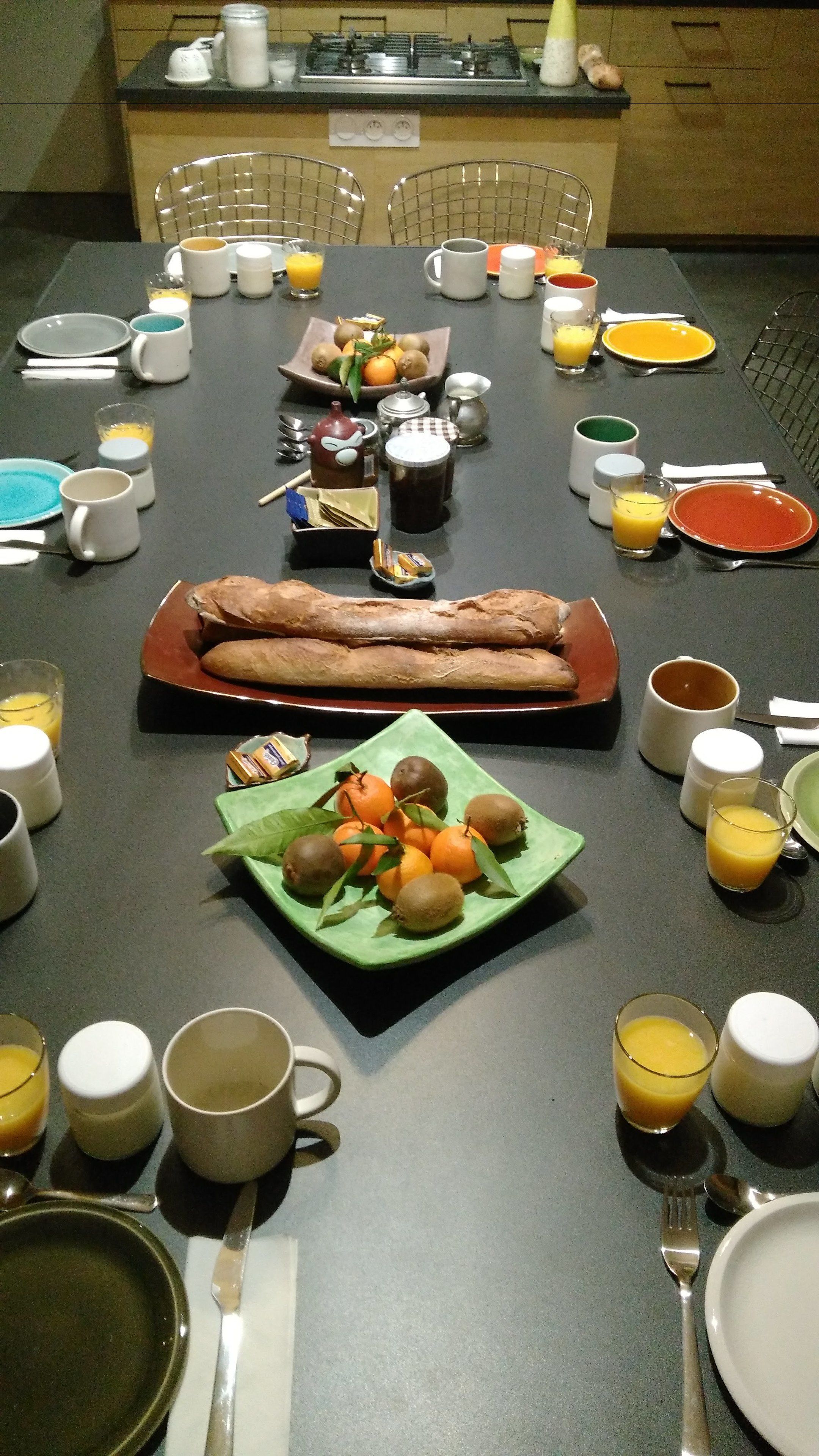 Mesa de jantar posta para o café da manhã com pão, frutas e bebidas.