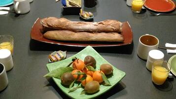 Mesa de jantar posta para o café da manhã com pão, frutas e bebidas.