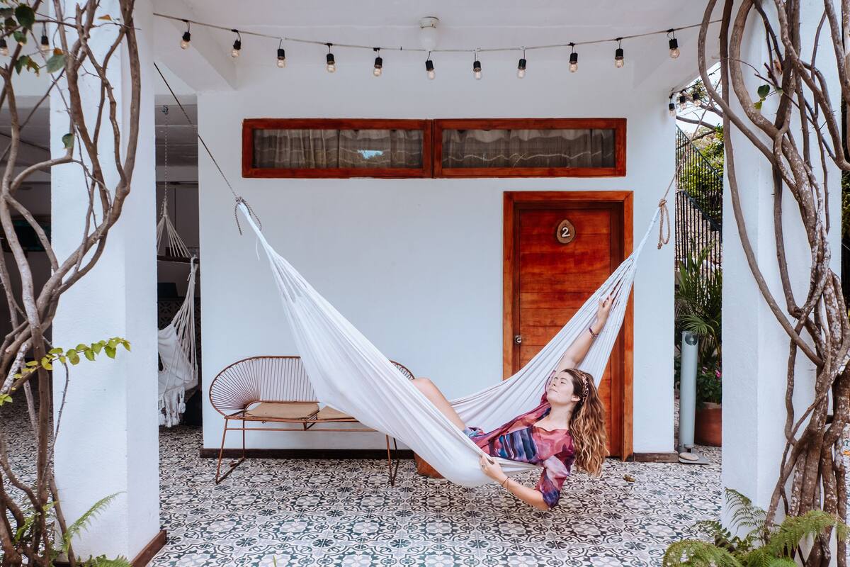 Uma mulher relaxando em uma rede em um quarto com piso estampado, uma porta de madeira e uma cadeira.