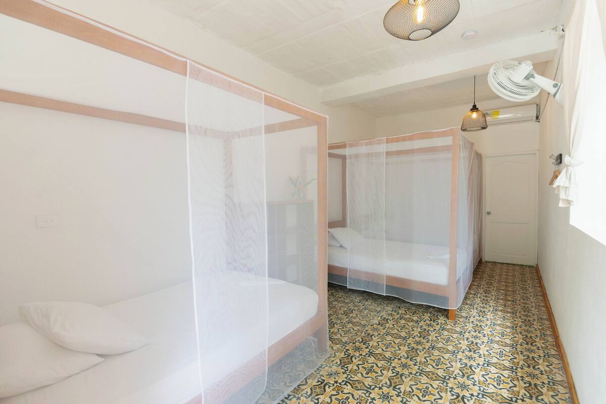 Quarto com duas camas, cada uma com mosquiteiro, piso estampado e ventilador de teto.