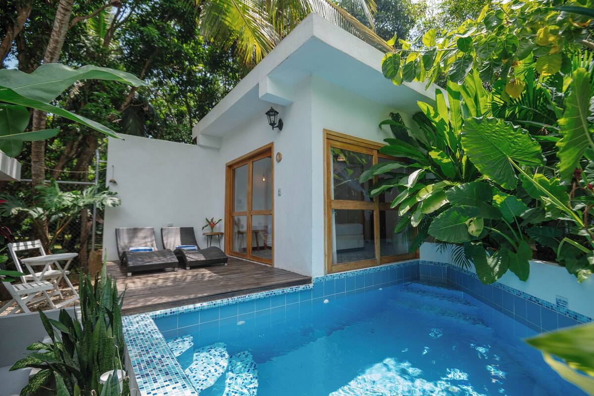 Uma área de piscina moderna com deck de madeira, espreguiçadeiras e porta de vidro que dá acesso a uma área coberta com assentos.