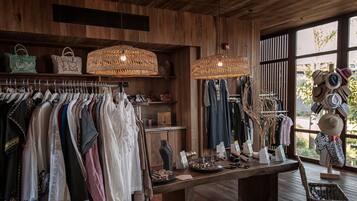 Loja de roupas boutique com interiores em madeira, araras de roupas e uma mesa expositora com acessórios.