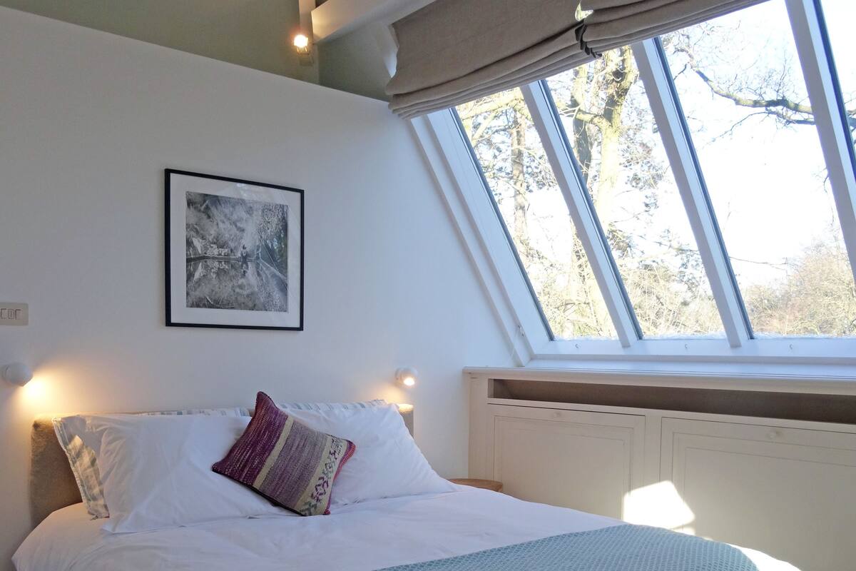 Quarto com cama, janela, radiador e quadro na parede.