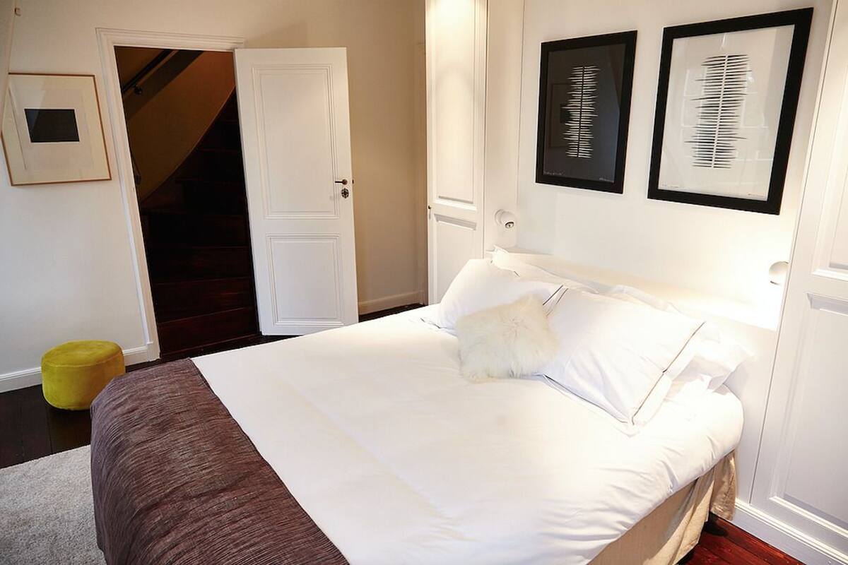 Quarto com cama, porta, escada e quadros nas paredes.