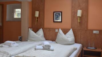 Quarto de hotel com duas camas, roupa de cama branca, um quadro na parede e uma mesa de cabeceira com copos.