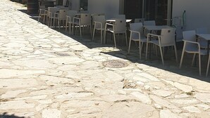 Um edifício com telhado plano, várias janelas e área externa pavimentada com mesas e cadeiras.