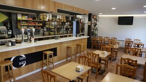 Um restaurante com área de bar, mesas e cadeiras de madeira e piso de azulejos.