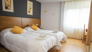 Uma cama de casal com almofadas brancas e amarelas, uma cabeceira de madeira e uma cama bem arrumada com uma toalha enrolada.