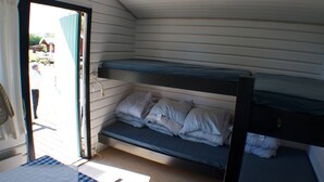 Quarto pequeno e compacto com uma cama beliche e uma cama de solteiro. O quarto tem teto inclinado e uma porta que dá para o exterior.