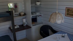 Quarto compacto com beliche, pequena cozinha, mesa de jantar com toalha quadriculada e luminária pendente.