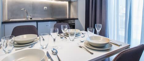 Uma sala de jantar moderna com uma mesa branca posta para quatro pessoas, incluindo pratos, tigelas, copos e talheres.
