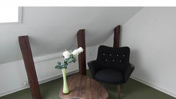 Um quarto com uma cadeira de madeira, uma mesa pequena e um vaso com flores brancas.